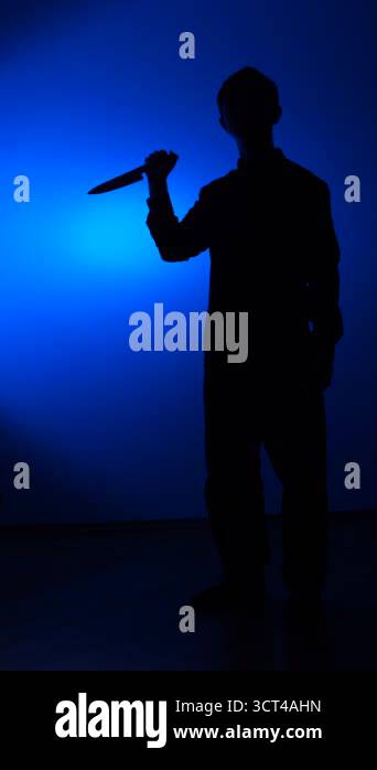 vertical video Silhouette of a man backlit by blue light raising a ...