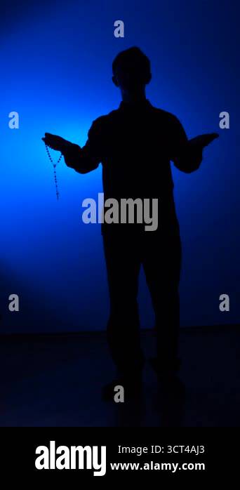 vertical video Man in silhouette holding a rosary bead in his hand ...