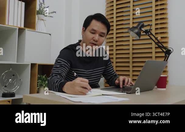 happy man writing document or paperwork with a laptop at home office ...