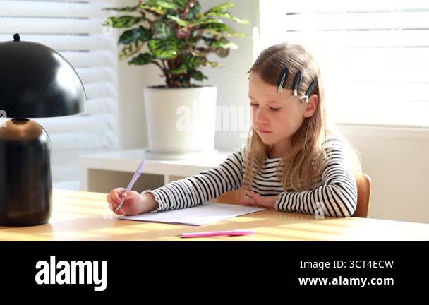 The cute girl writes carefully and intently at home at the table. The ...