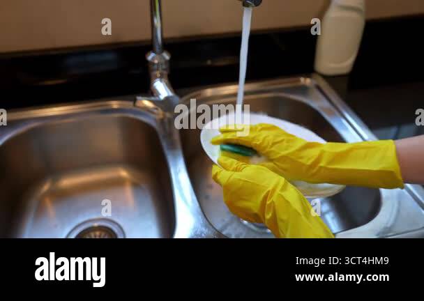 Hand in yellow gloves scrubbing a white plate with sponge and detergent ...