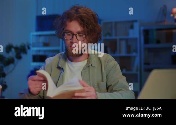 Young Man Reads Book with Deep Focus in Evening Study Environment ...