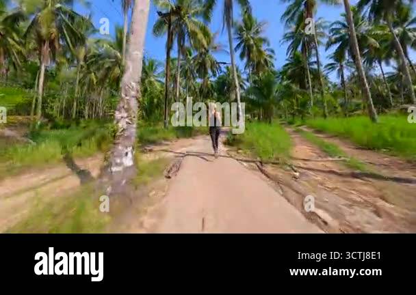 Cinematic FPV drone shot of fit woman running on path through tropical ...