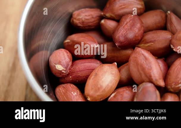 Shelled roasted peanuts in brown skins arranged in metal container on ...