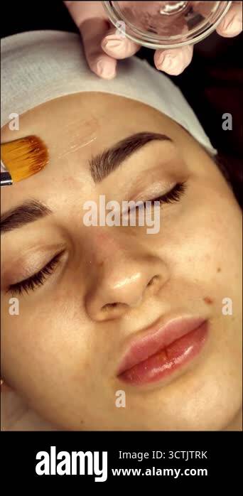 A beautician applies a cosmetic product to a womans forehead with a ...