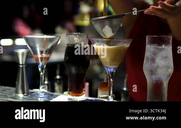 barista shaking iced black coffee in shaker and pouring in cocktail ...