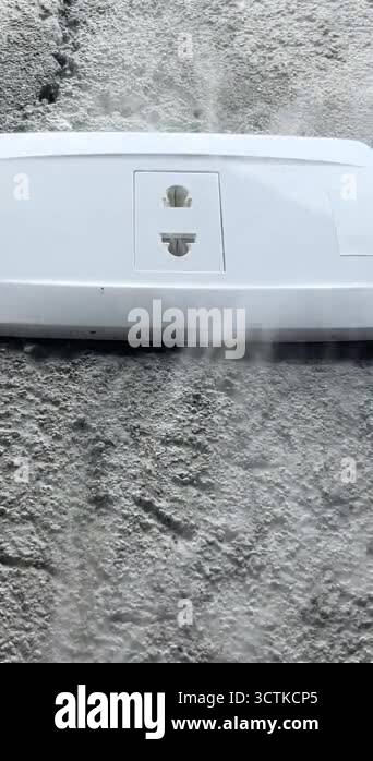 A smoking electrical outlet on a gray concrete wall from overvoltage ...