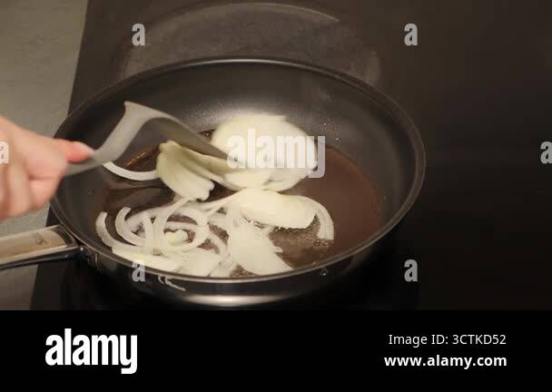 Female hand stirs sliced onion rings in frying pan with sunflower oil ...