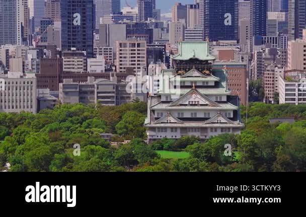 Slow sweeping aerial view of Osaka Castle surrounded by green trees ...