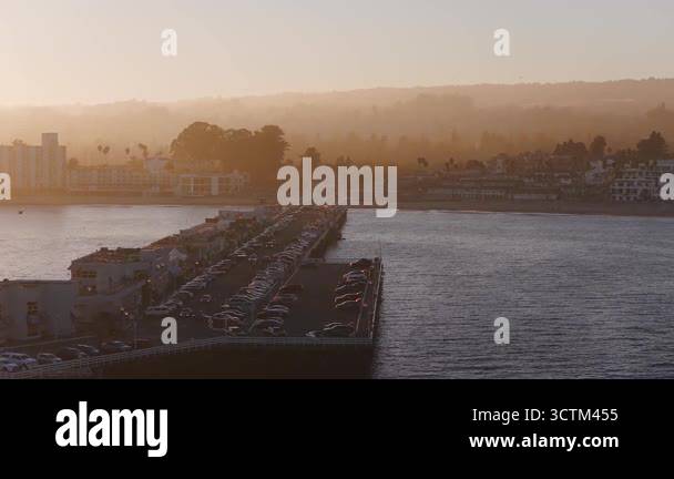 Serene aerial view of Santa Cruz pier at sunset, with parked cars, calm ...