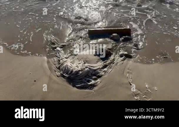 A wave washes over trash and remnants of plastic bags on the shore of ...