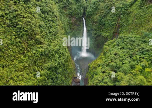 Tall waterfall plunging into mist surrounded by dense tropical ...