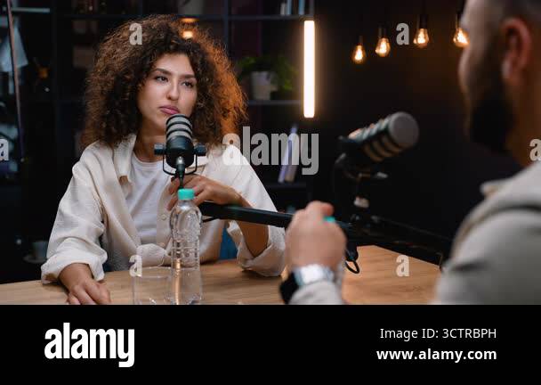 Expressive curly haired woman speaking into a professional microphone ...