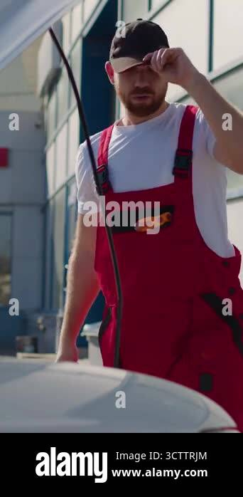 Male mechanic in red overalls checks engine and fluid levels under the ...