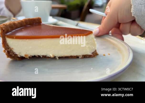 A womans hand is spooning cheesecake in front of a cellphone that is on ...
