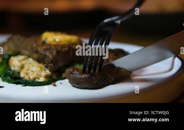 Close-up shot of a knife and fork slicing through a grilled steak on a ...