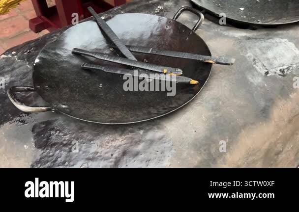 Metal wok with wooden sticks placed inside over clay stove in outdoor ...