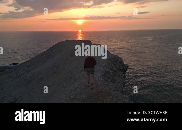 Woman walks out on narrow cliff edge to view the setting sun at Cape St ...