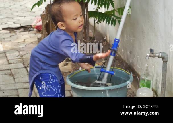 A young toddler is happily learning to walk and is playing in a water ...