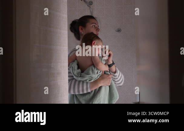 Mother combing baby's hair while holding child wrapped in towel after bath, tender family moment ...