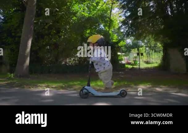 Toddler with yellow helmet crying loudly while riding scooter on park ...