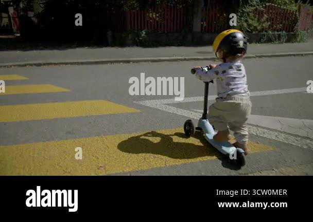 Toddler crossing street on scooter with yellow helmet, joyful childhood ...