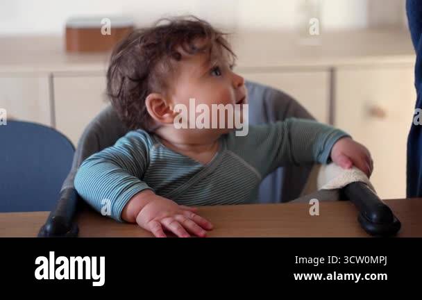 Baby sitting in high chair looking up at parent, everyday family ...