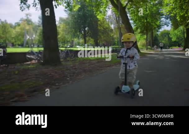 Toddler falling off scooter on park path while wearing helmet, child ...