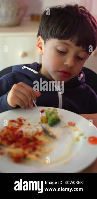 Boy eating vegetables at dining table, opening mouth wide while using ...