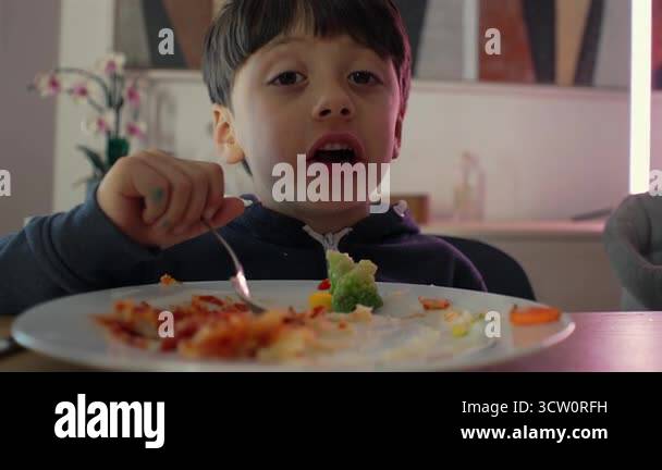 Young boy chewing food while looking directly at camera during family ...