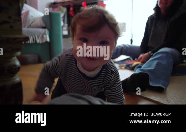 Smiling toddler crawling toward camera on wooden floor while mother ...