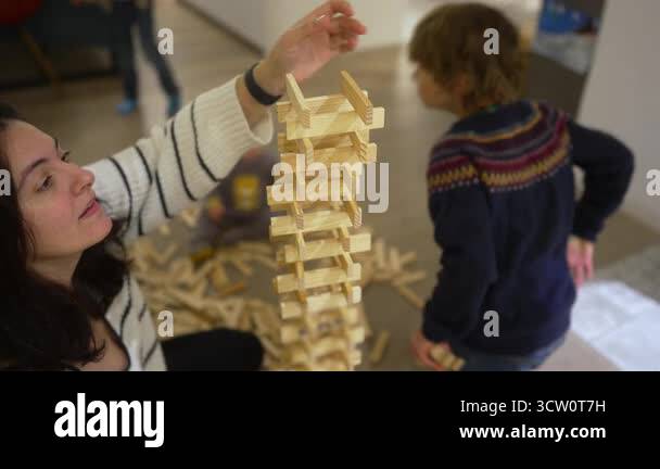 Close up of child carefully placing wooden blocks on tower while family ...