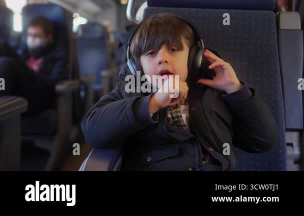 Child wearing headphones on train singing into hand, young boy immersed ...