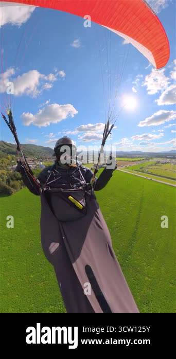 Paragliding free flight on a red wing soaring above green countryside ...