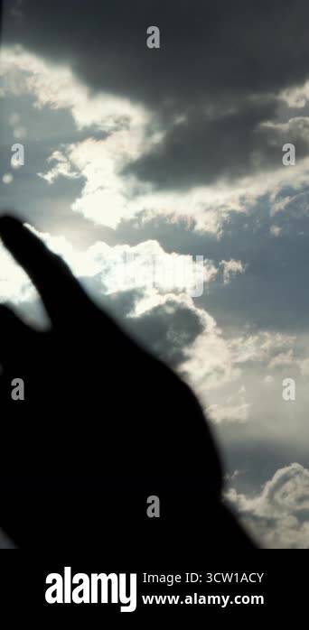 Silhouette of a hand reaching toward the sun as rays of light pierce ...