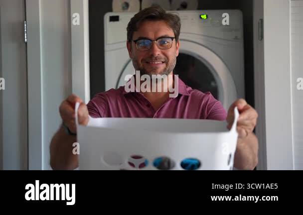 Man with glasses smiles while holding laundry basket in front of ...