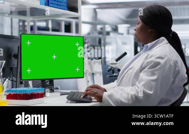 Green screen desktop next to black woman researcher performs bio ...