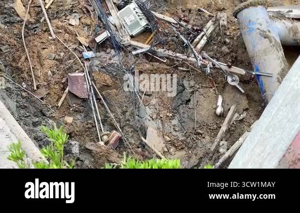 A severe road collapse with broken asphalt, exposed soil, and fallen ...