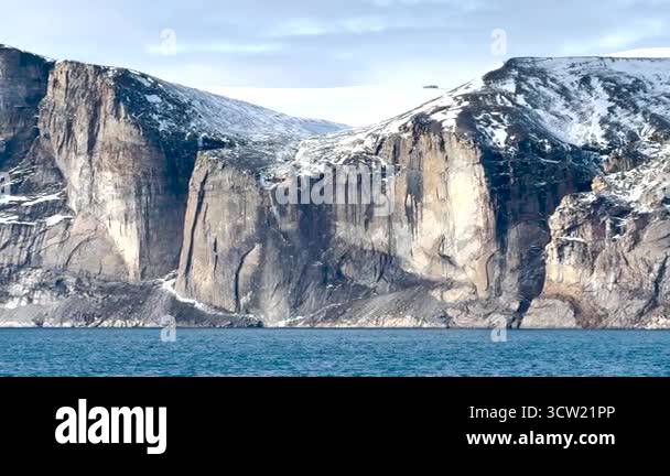 Snow blankets dramatic cliffs along a tranquil sea, reflecting the ...