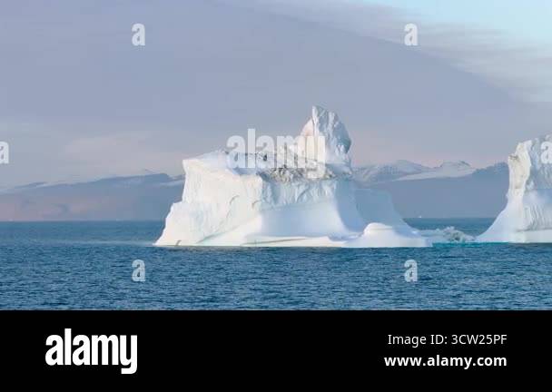 A large iceberg glides smoothly on clear blue waters during early ...