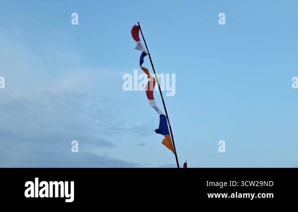 Footage of colorful triangular flags waving in the wind on a tall pole ...