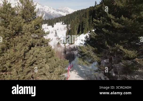 Aerial revealing backwards view narrow ski slope lined with trees ...
