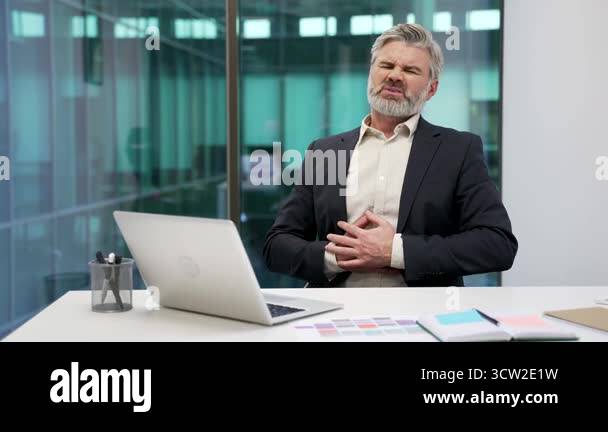 Unhealthy mature businessman feels stomach pain sitting at workplace in ...