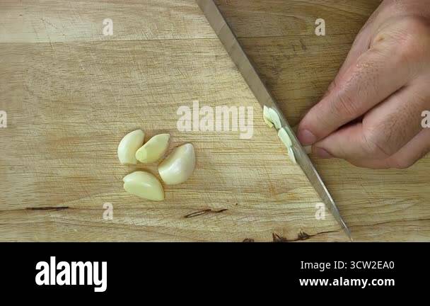 Man hands chopping raw garlic on a scratched wooden cutting board with ...