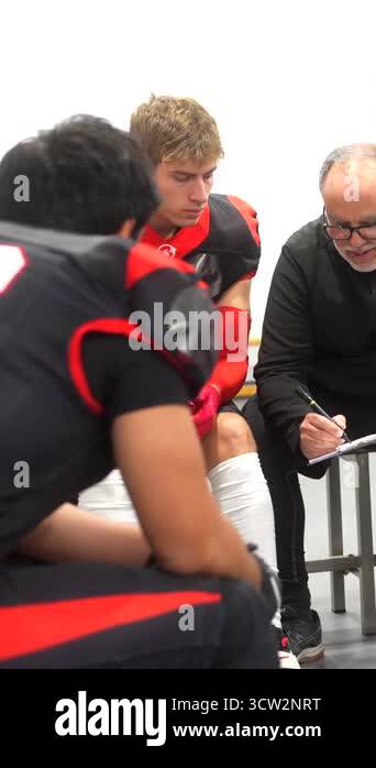 Focused football players sitting on a bench in a locker room, intently ...