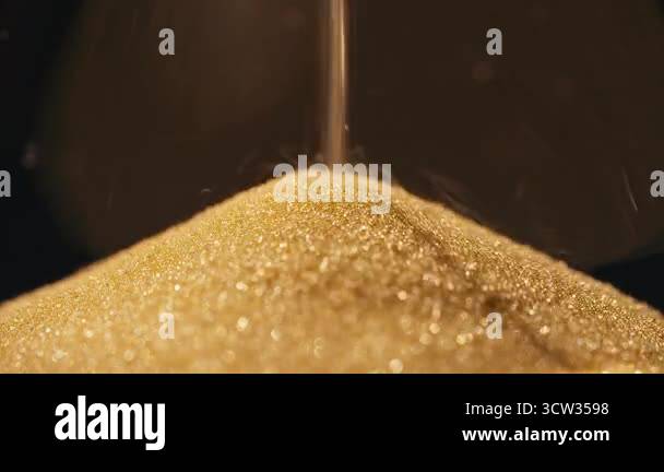 Close-up photograph of golden glittering sand leaking out of an ...
