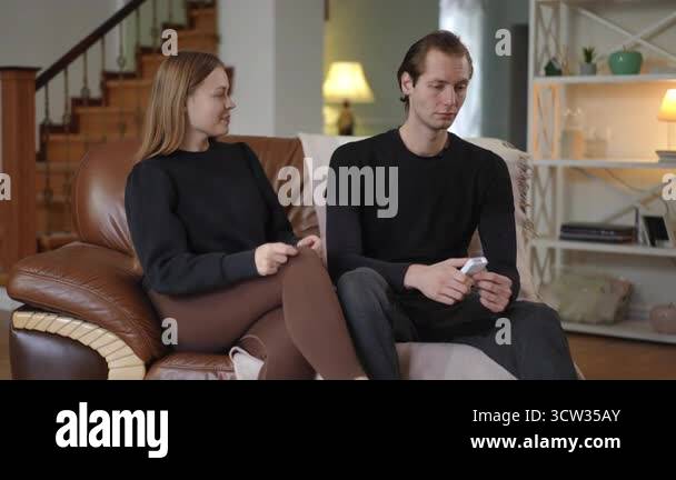 A woman looks at her husband with a conciliatory smile, trying to ...