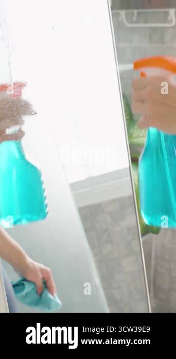Vertical video. Woman applying blue glass cleaner to tall mirror in ...