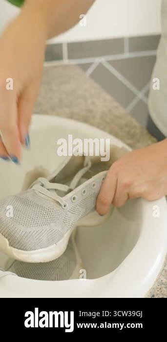 Vertical video. Woman removing laces from light grey sneaker over small ...