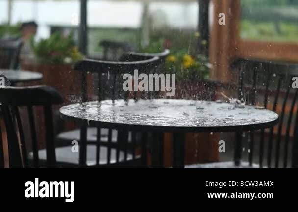 Round outdoor table with chairs covered in rainwater. Drops splash ...